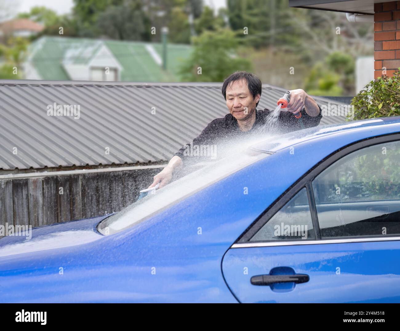 Man washing car windows in the front yard using a brush and water spray ...