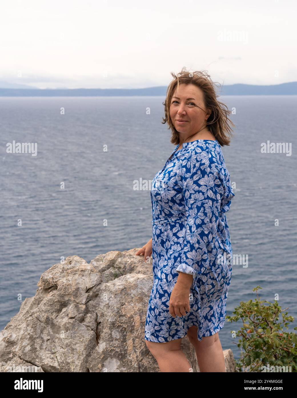 Middle aged lady on steep seashore, enjoying the sea, the sun, life ...
