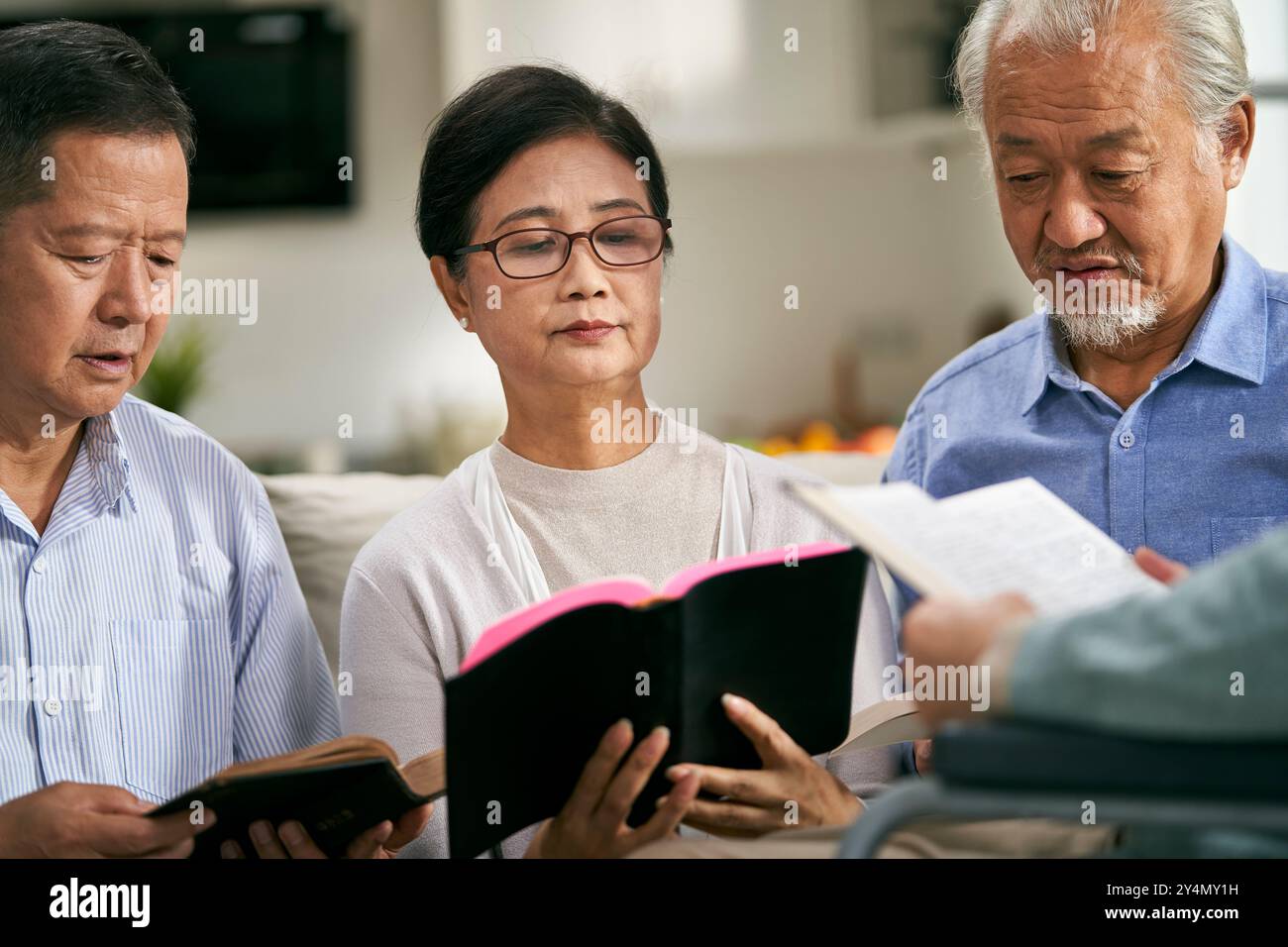 group of asian senior people sitting on couch at home reading bible ...