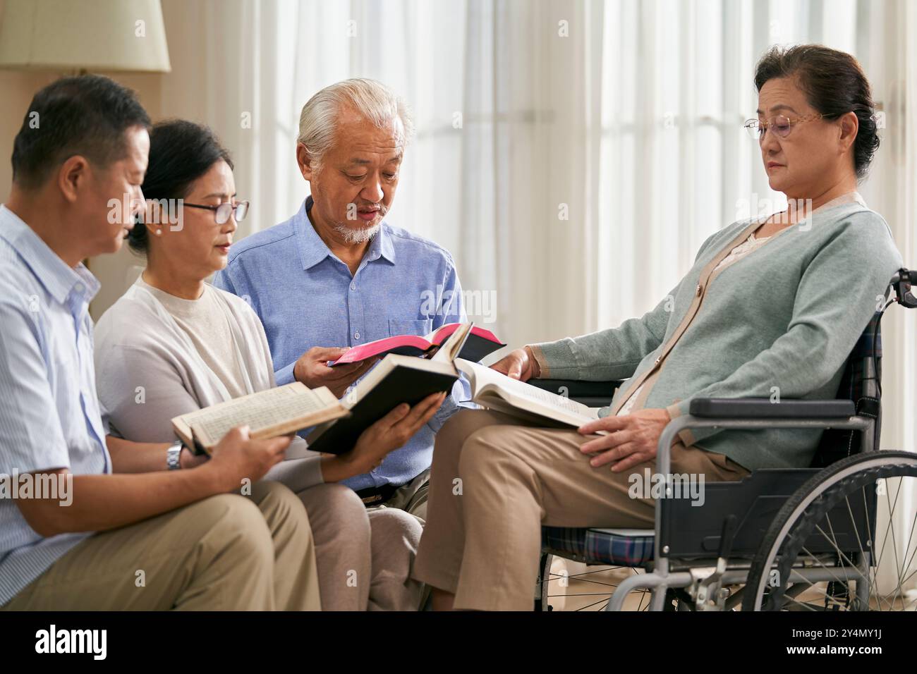 group of asian senior people sitting on couch at home reading bible ...