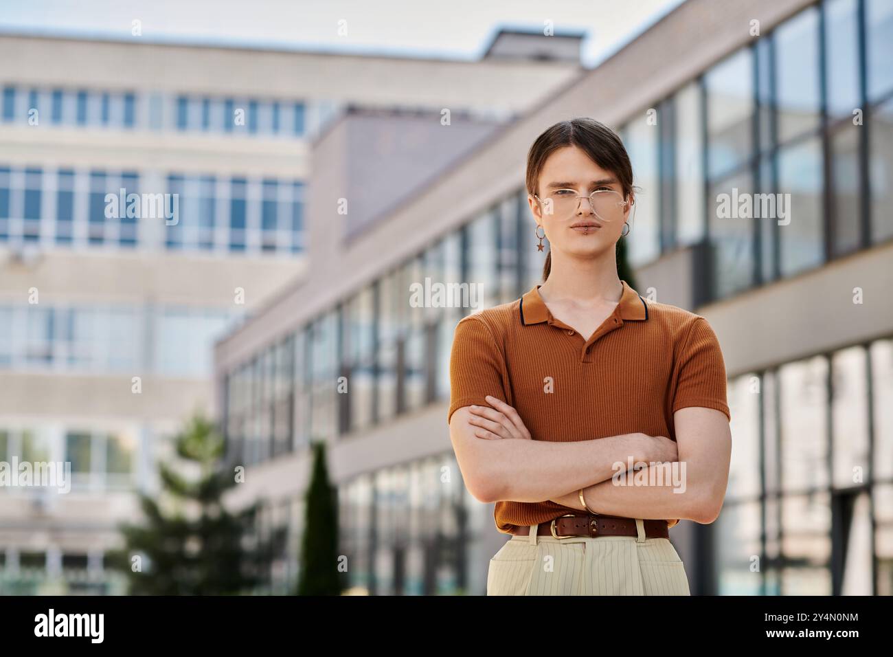 A young non binary person stands confidently with crossed arms in a ...