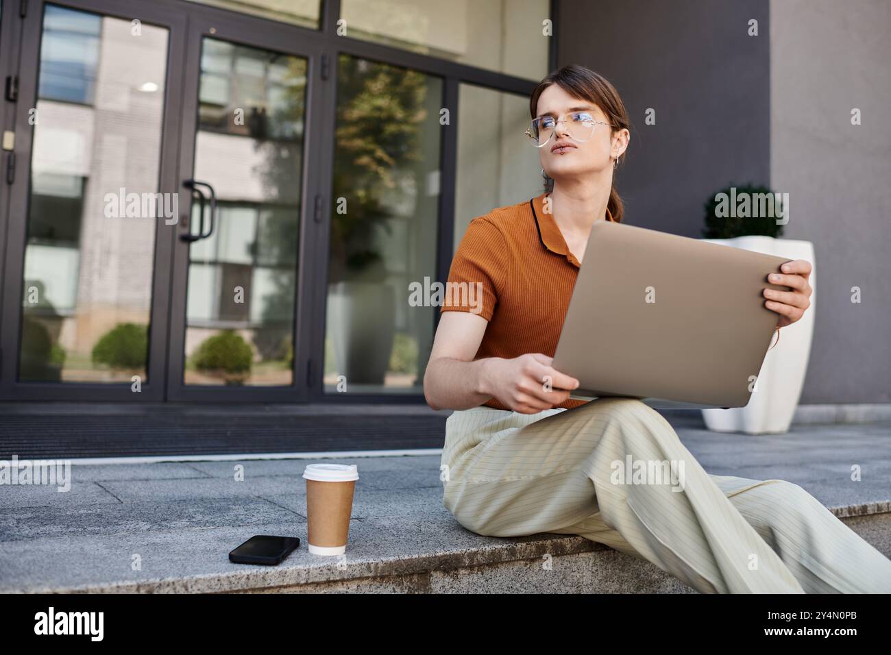 A young non binary individual sits outside an office, thoughtfully ...
