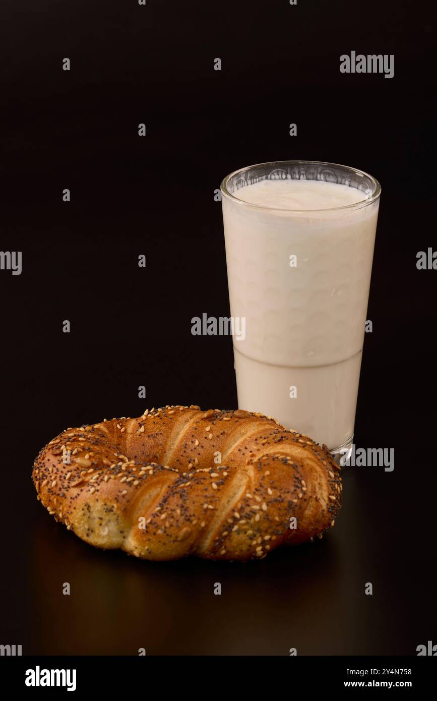 a pretzel with mixed seeds and a glass of kefir on a black background ...