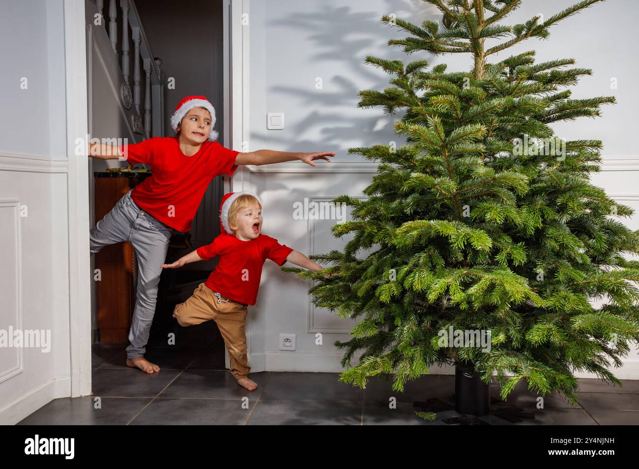 Toddler and his brother peer from doorway beside Christmas tree Stock ...