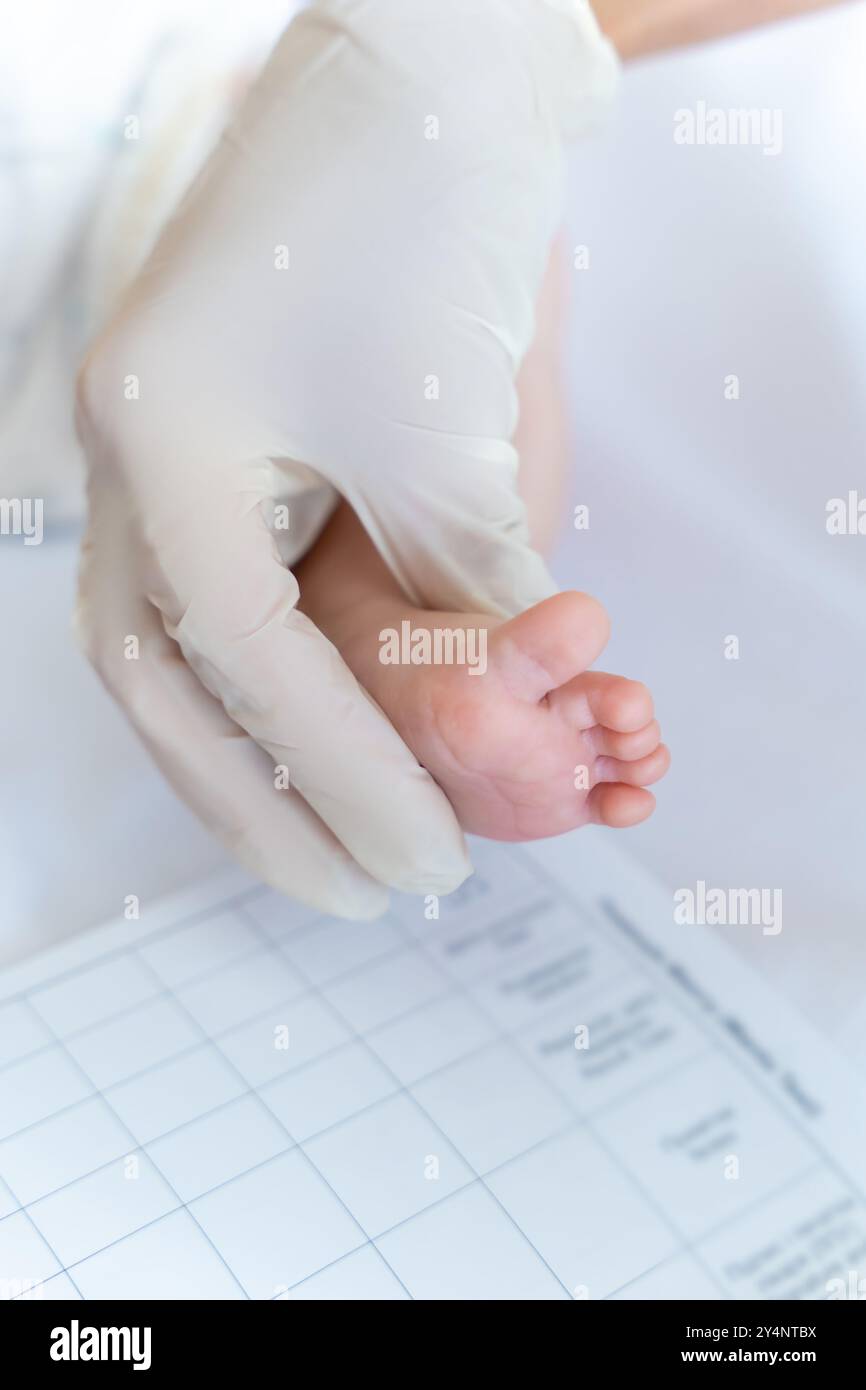 Doctor wearing rubber gloves checking newborn’s feet in healthcare ...