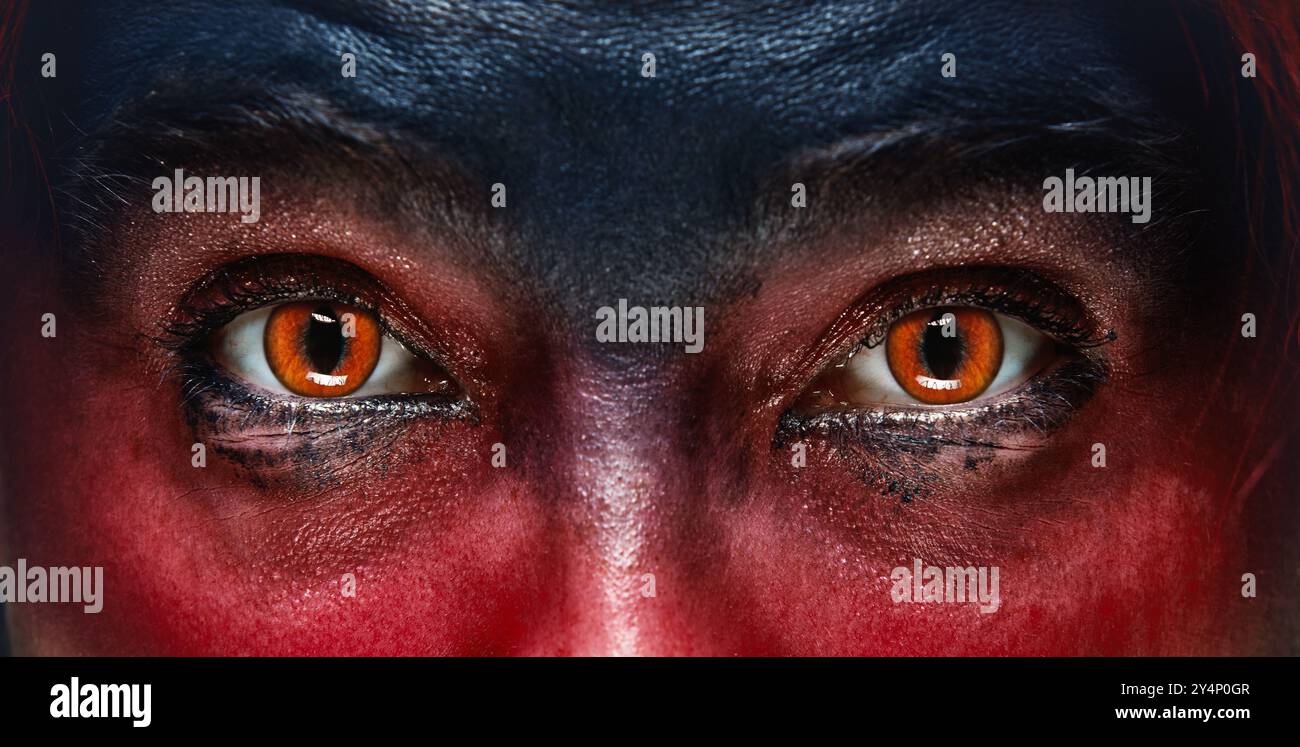 Close-up of a woman glowing demonic eyes with face partially painted in red and black. Demonic ...