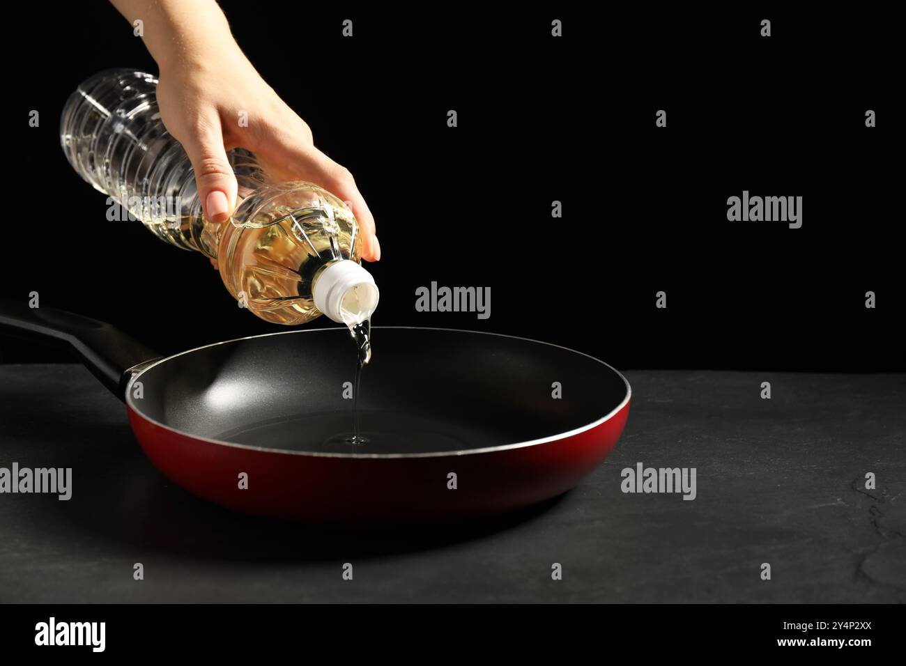Woman pouring oil into frying pan at dark gray textured table against ...