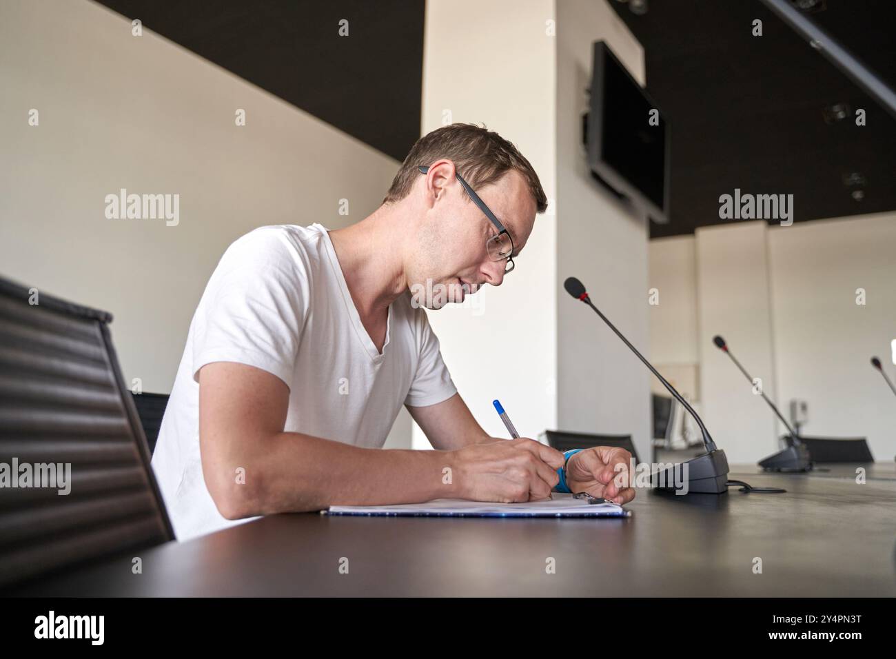 Focused male delegate writing notes at conference table with ...