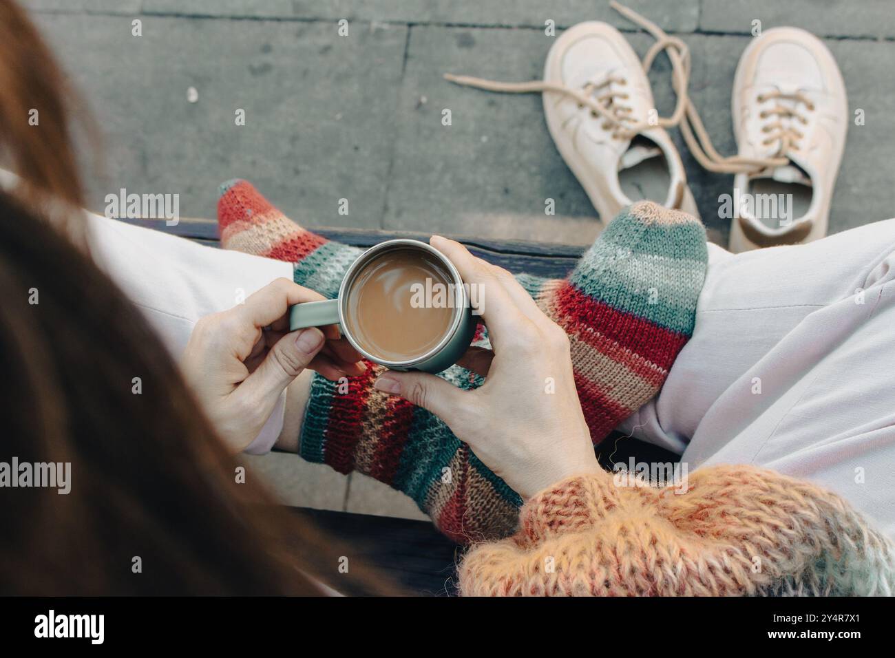 Woman with coffee cup sitting on bench in knitted clothes, top view ...
