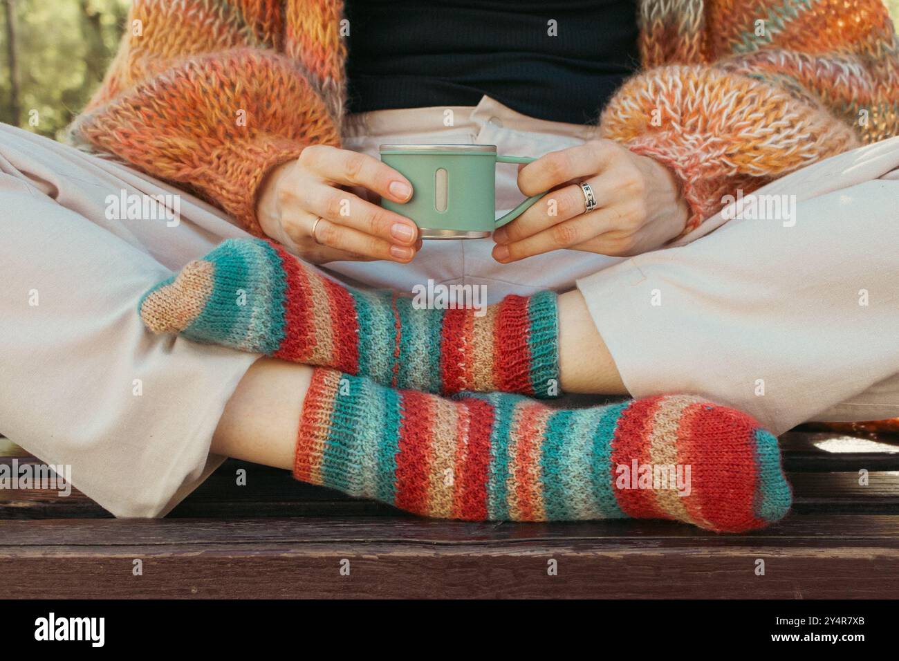 Woman with coffee cup sitting on bench in knitted clothes, top view ...