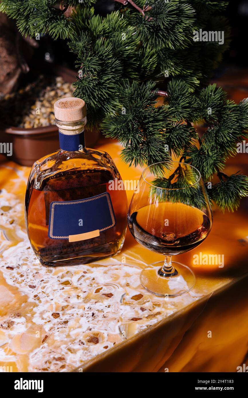Bottle of brandy and a filled glass set against a pine tree backdrop ...