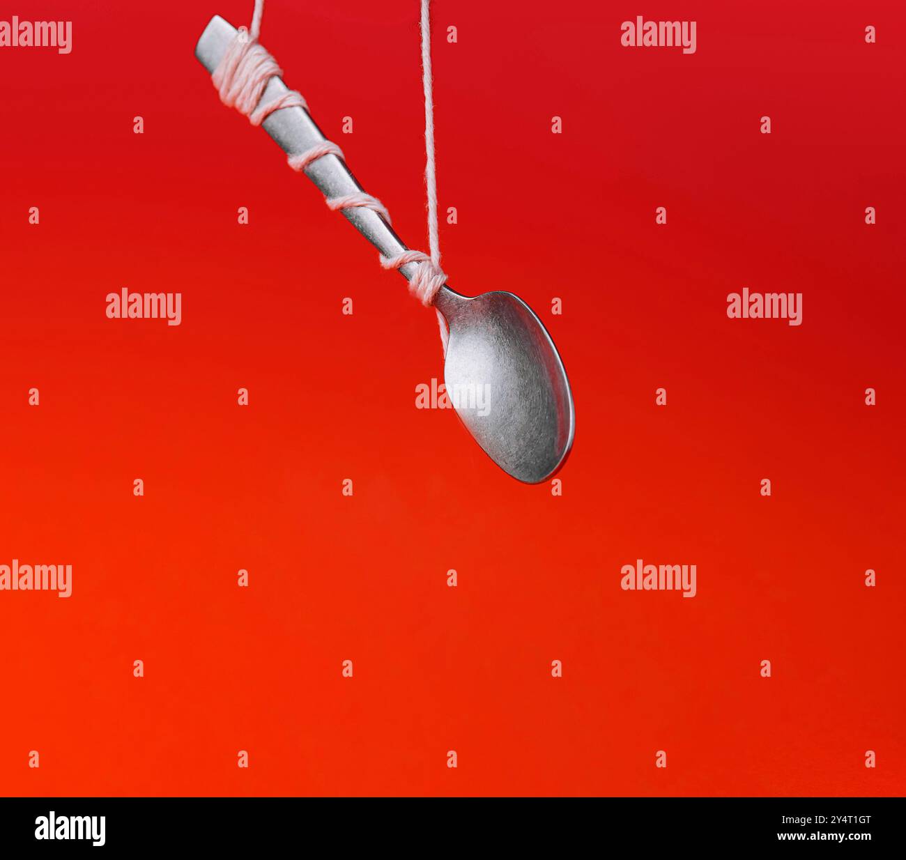 Silver spoon tied with string against a vibrant red backdrop, creating ...