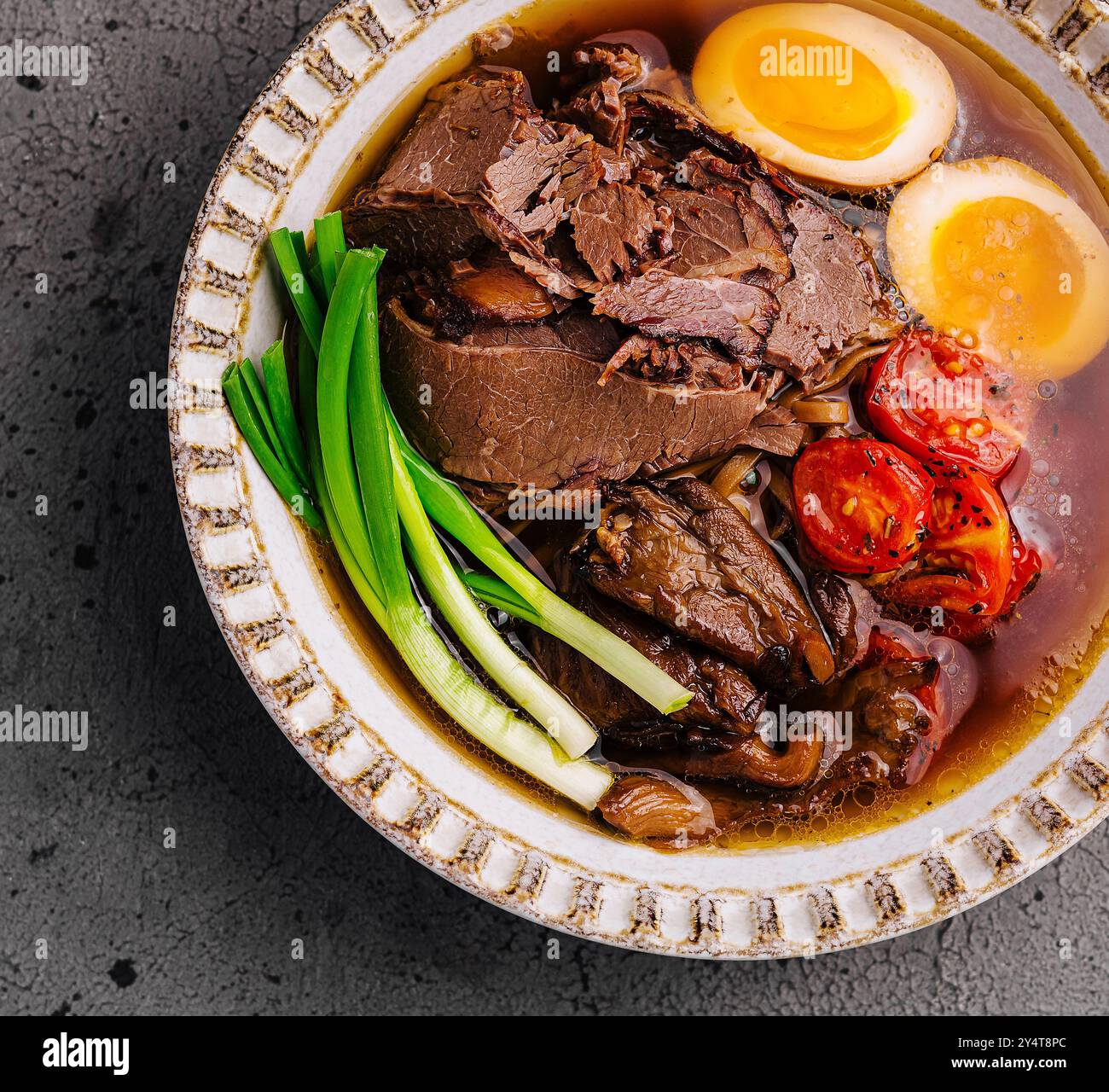Traditional beef ramen with soft-boiled egg, tomatoes, and green onions ...