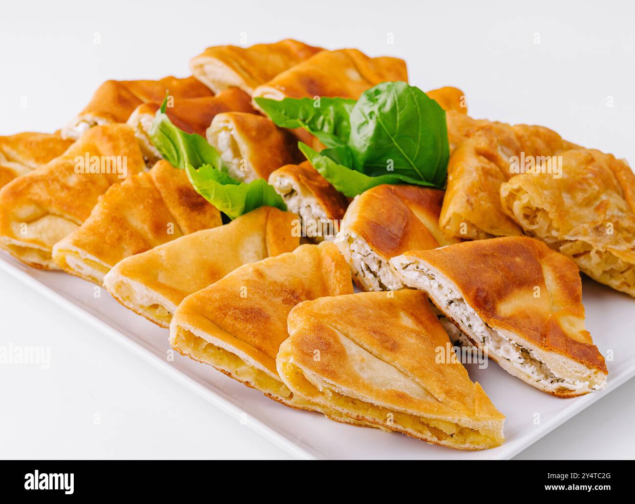 Selection of golden puff pastries served with basil garnish on a white ...