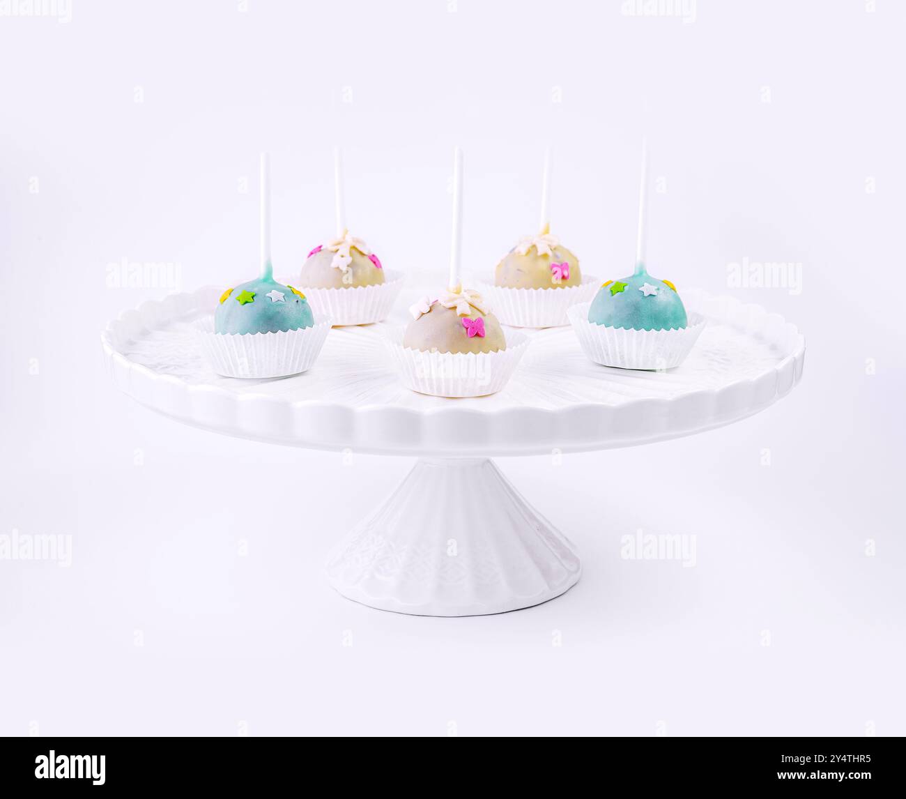 Assorted cake pops with colorful sprinkles displayed on a stylish white ...