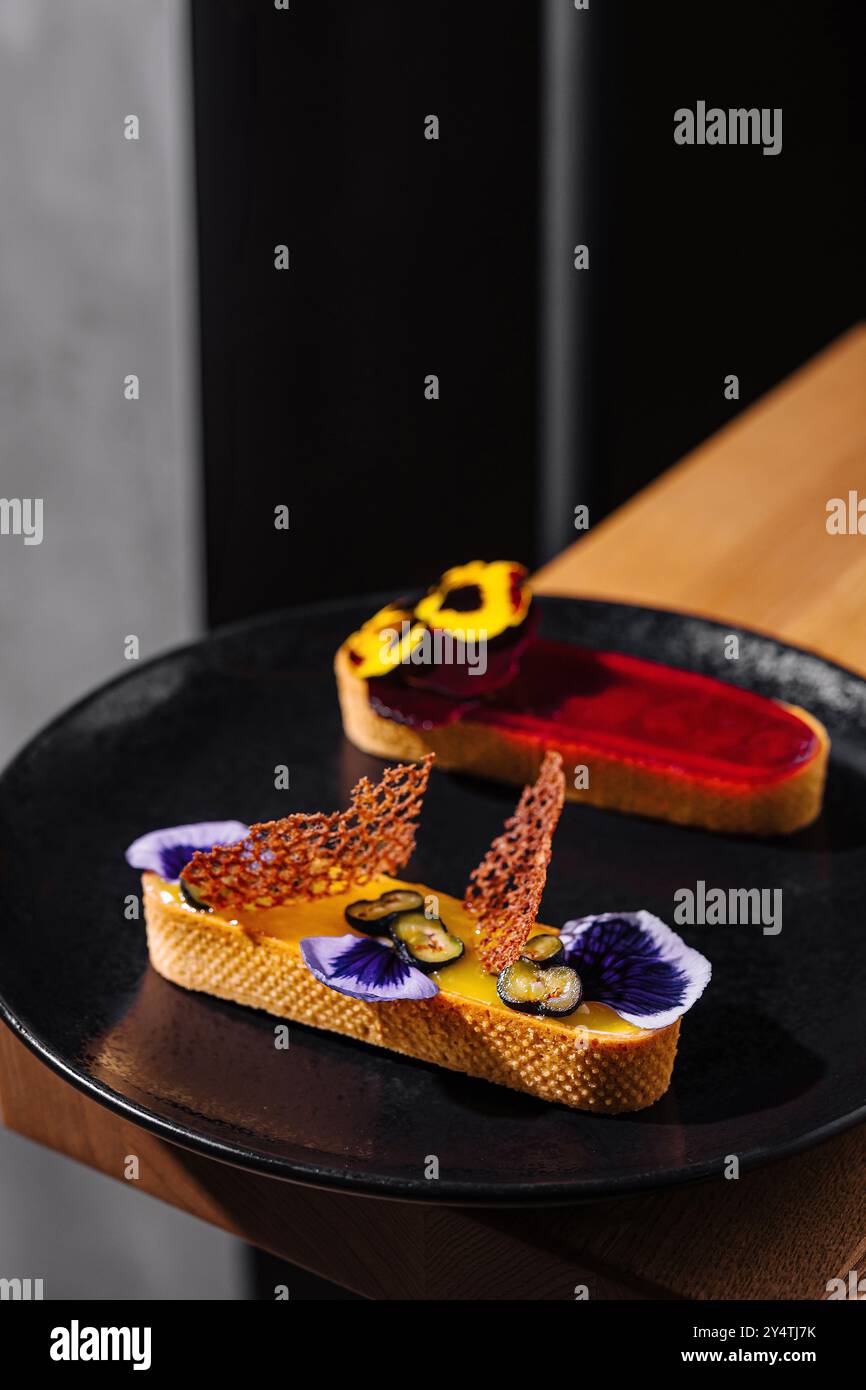 Elegant dessert with vibrant garnishes served on a sleek black plate ...