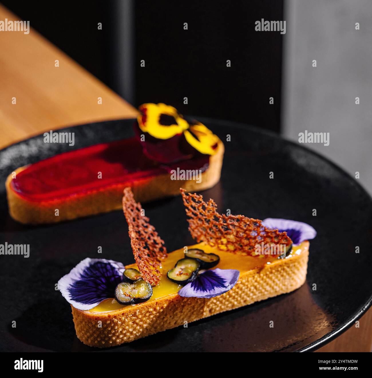 Elegant dessert with vibrant garnishes served on a sleek black plate ...