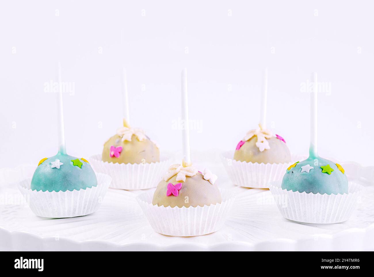 Assorted cake pops with colorful sprinkles displayed on a stylish white ...