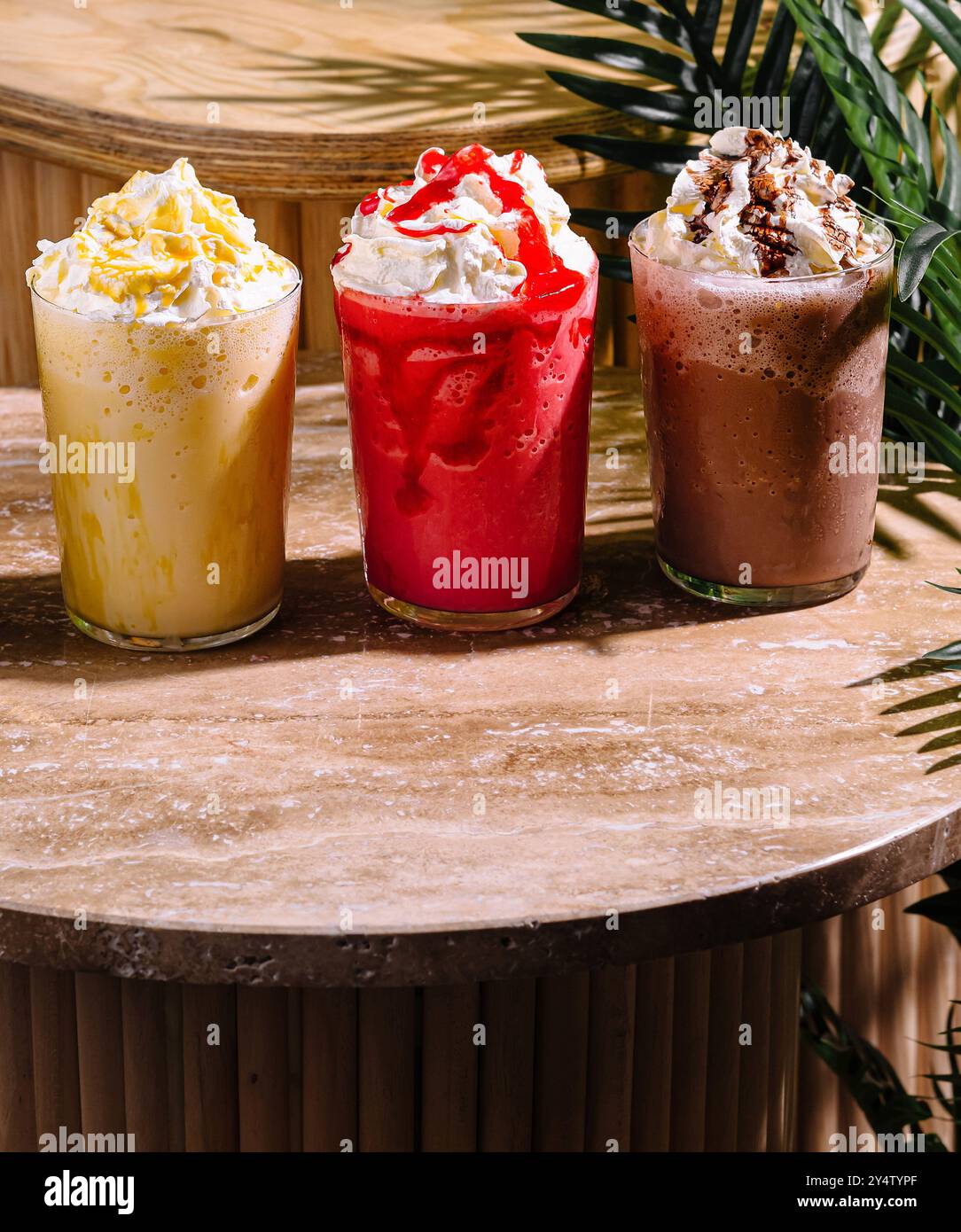 Three milkshakes with different flavors toppings are sitting on table ...