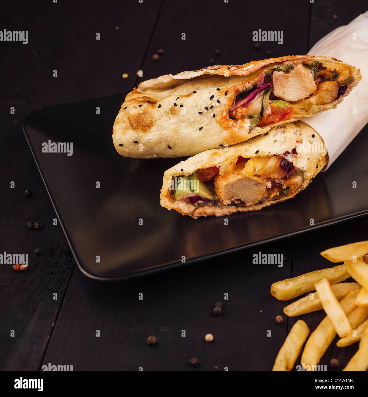 Chicken shawarma wrap cut in half lying on a black plate with french ...