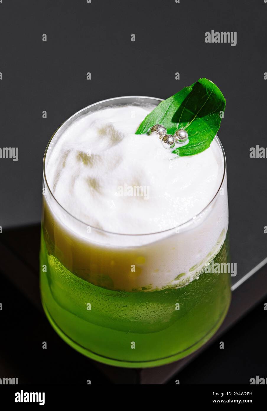 Green cocktail with egg white foam and basil leaf garnish is standing ...