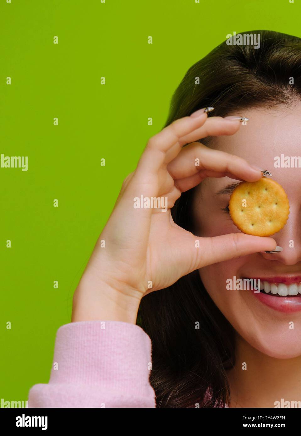 Young woman is holding up a salty cracker in front of her eye and ...