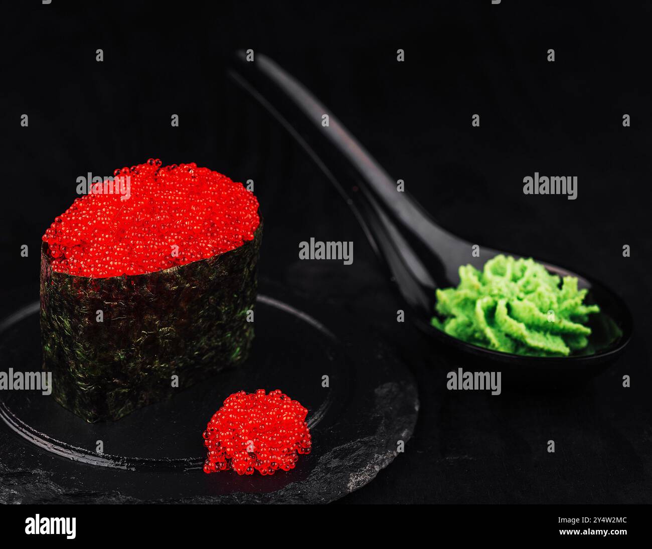 Gunkan maki sushi with tobiko flying fish roe is presented on a black ...