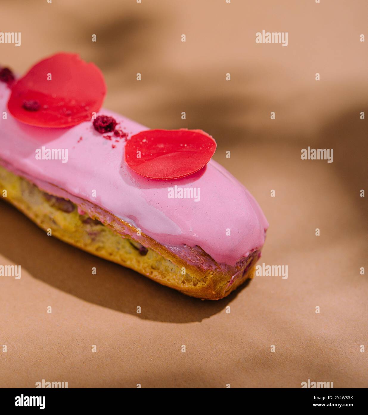 Gourmet pink eclair with delicate toppings on a subtle beige backdrop ...