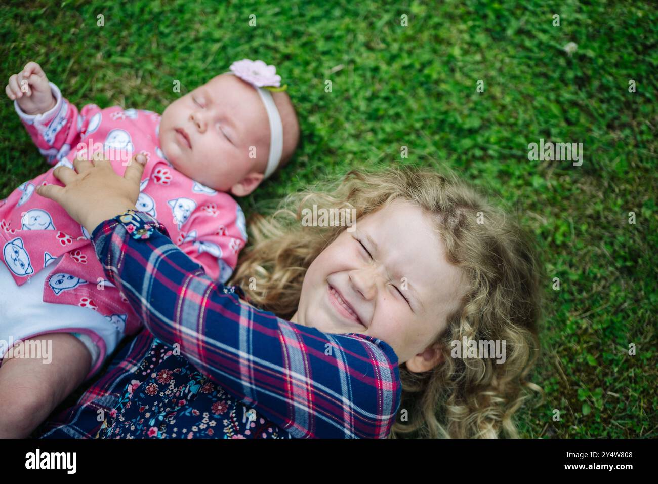 Big sister making silly faces while laying on the grass with her little ...