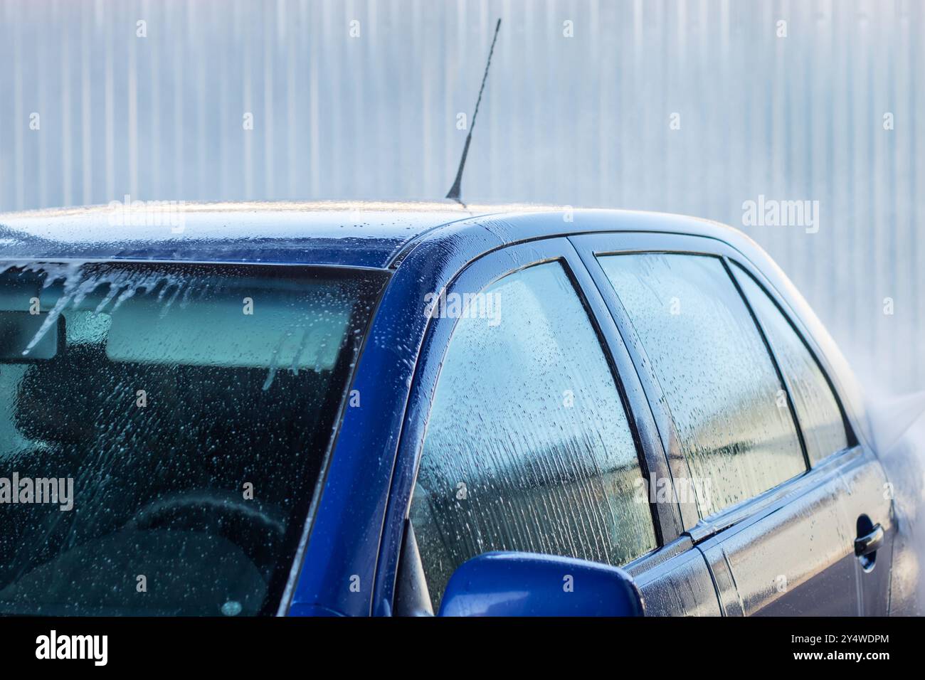 A blue car is currently undergoing a thorough washing process with soap ...