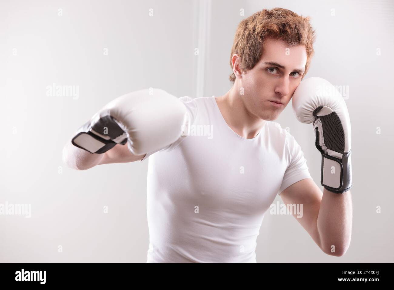 White male boxer in white, geared up with boxing gloves, stands poised ...