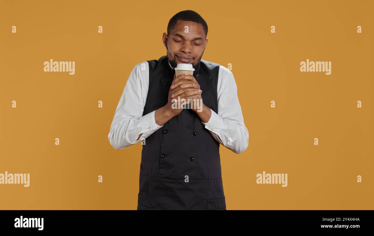 Cheerful waiter drinking a cup of coffee and relaxing after serving ...
