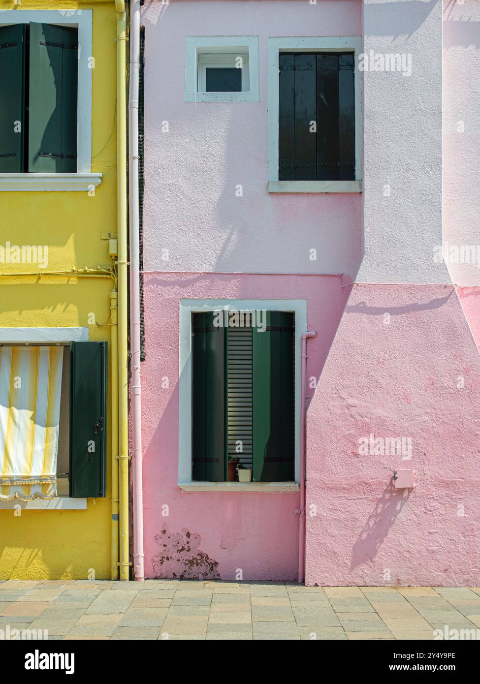 Colorful yellow and pink house walls with green shuttered windows on a ...