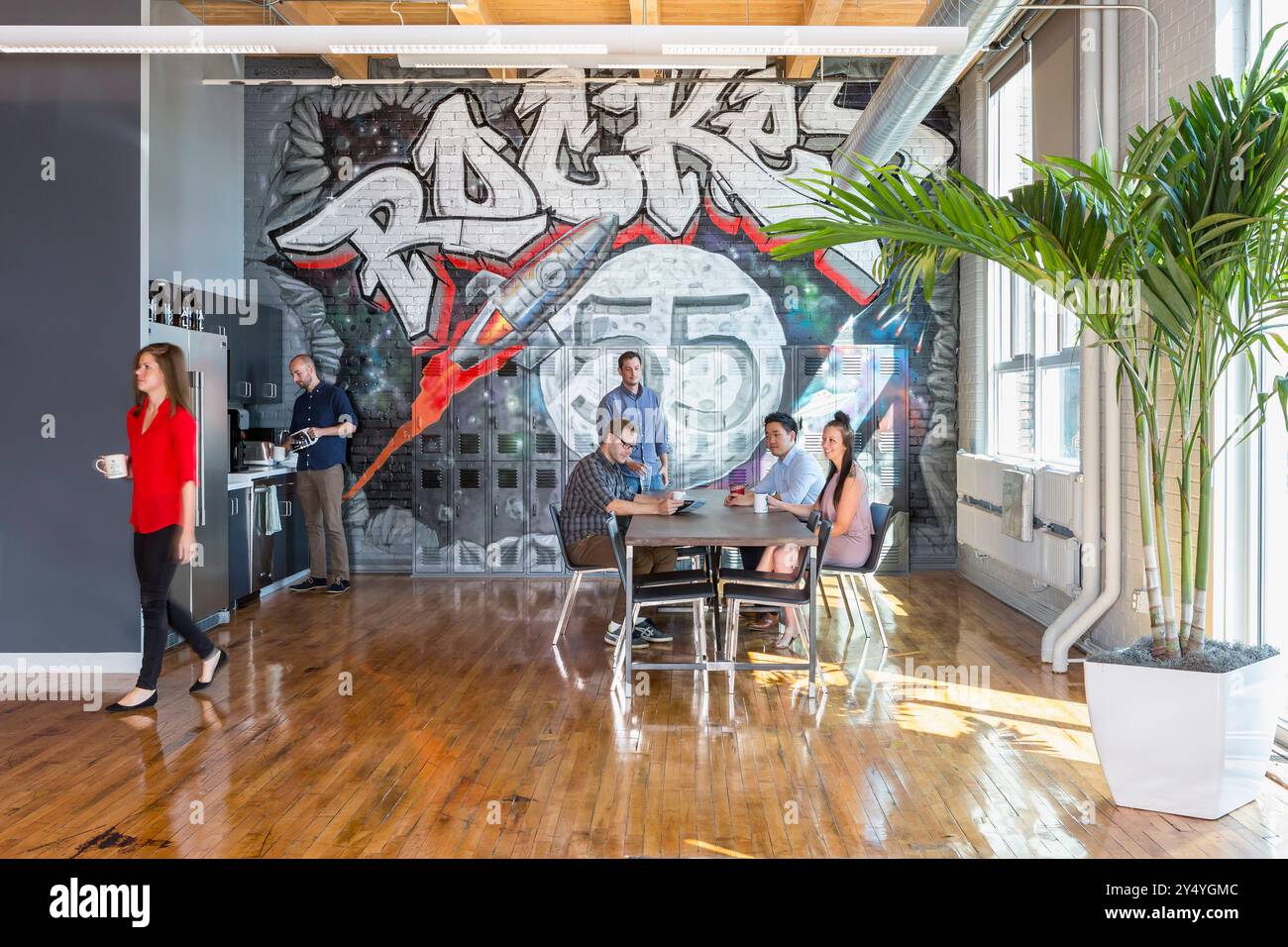 Employees gathered in colorful office lunchroom with grafitti style ...