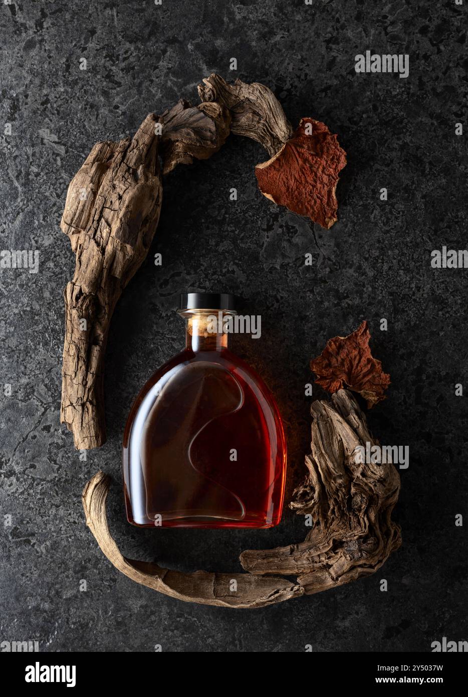 Bottle of brandy and old snags with dried up vine leaves on a black ...