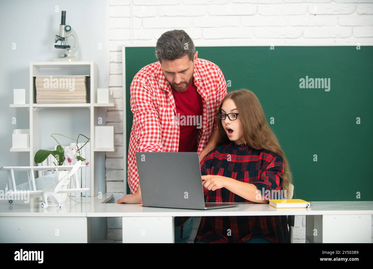 Teacher helping school kids in classroom at school, using computer ...