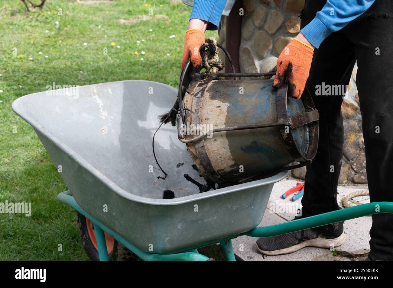 A man pours mud from a bucket into a wheelbarrow from the bottom of a ...