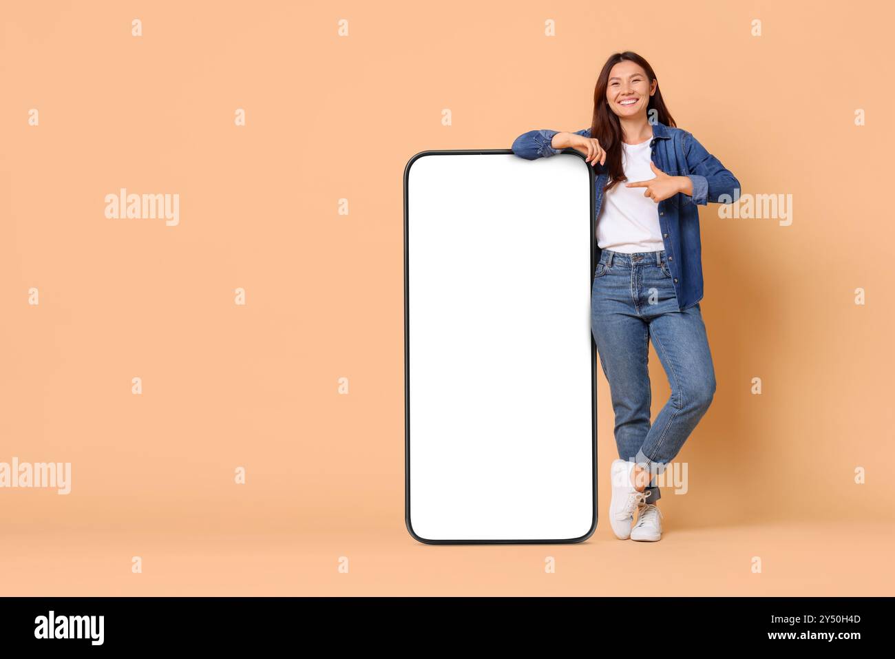 Happy smiling woman pointing at big mobile phone with blank screen on ...