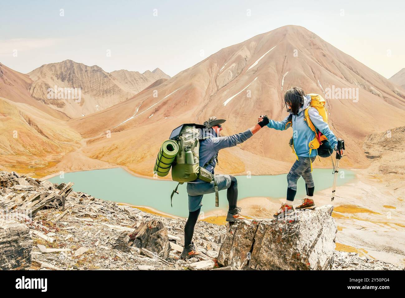 Strong woman give hand helps her man climb rock in mountains. Two family team people climb to ...