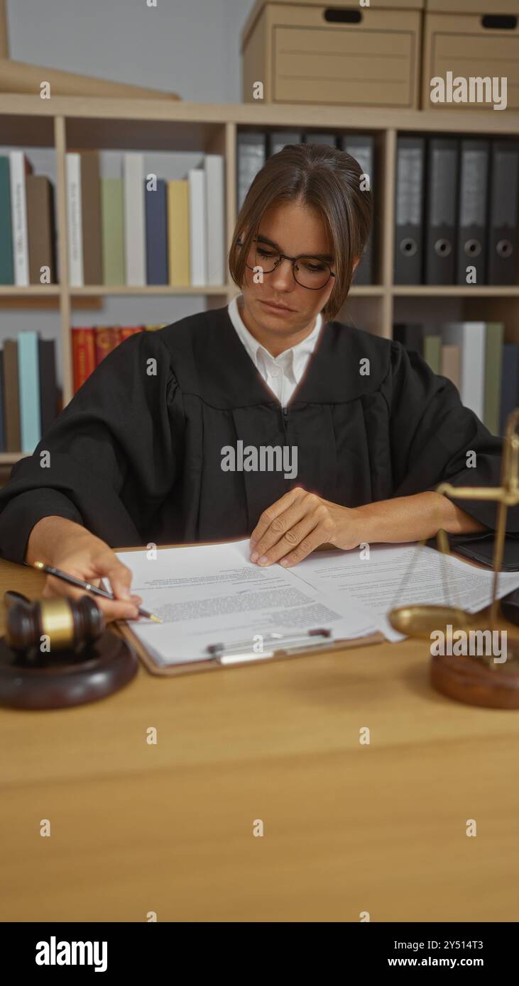 Young hispanic woman judge writing in courtroom with glasses and gavel ...