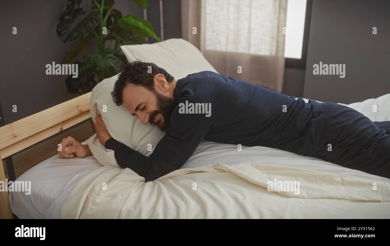 Bearded man smiling comfortably on a bed in a bedroom with natural ...