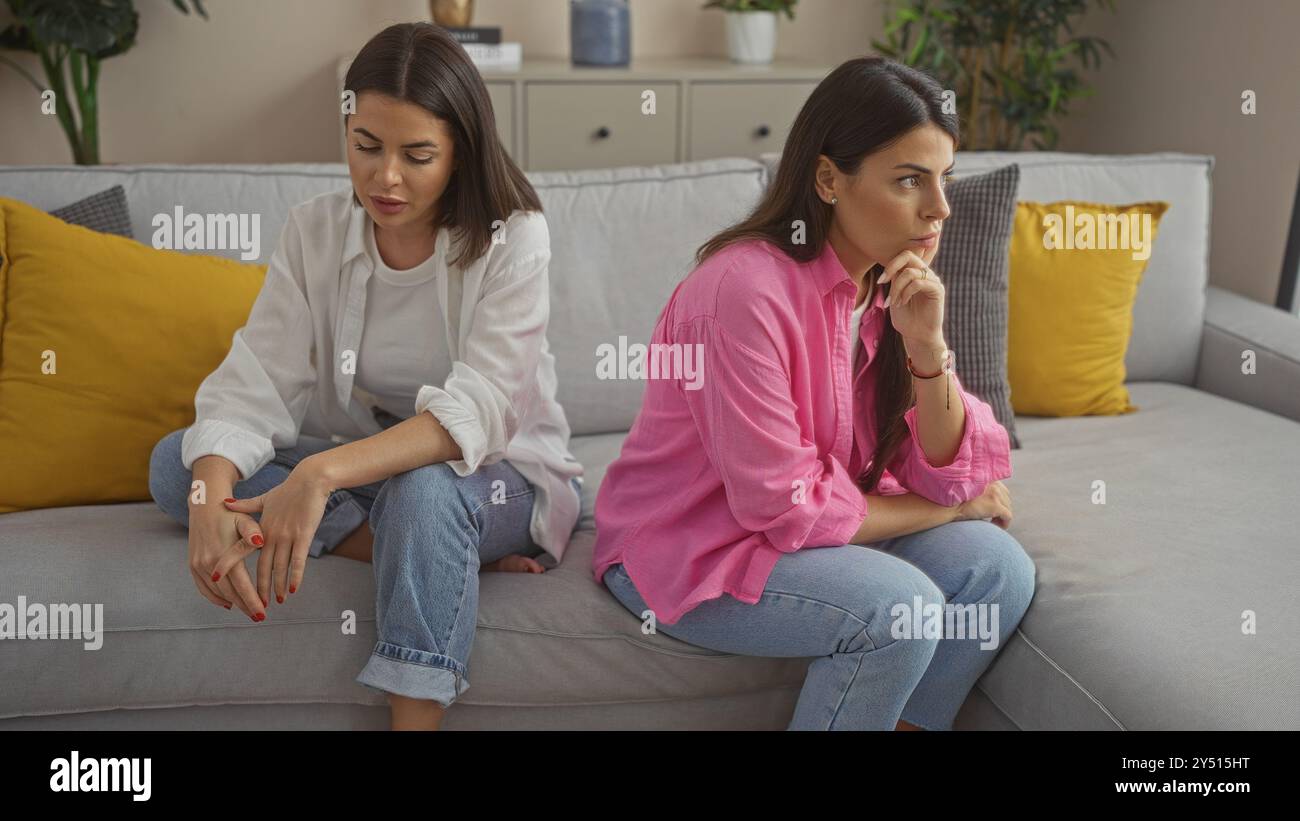 Two hispanic women sit together in a living room, appearing thoughtful ...