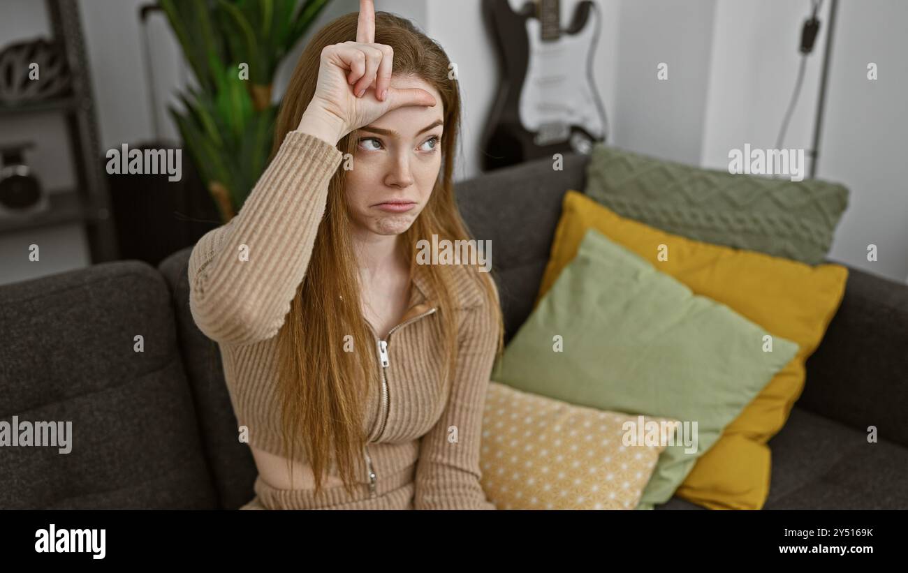 A young blonde woman gestures a loser sign in a stylish living room ...