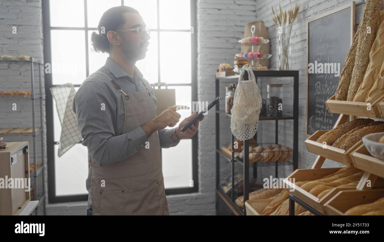 Hispanic man with moustache working in a bakery shop, using a tablet to ...