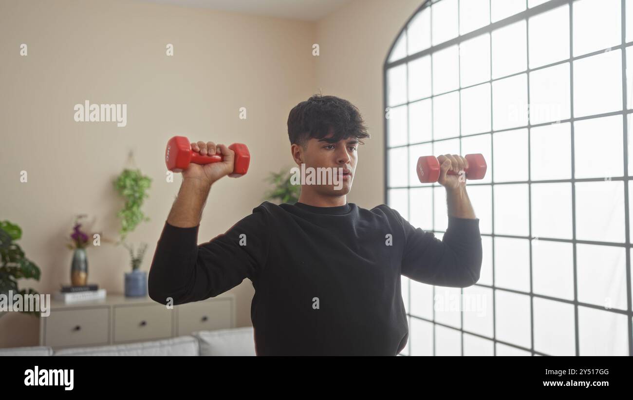 A young hispanic man exercises with dumbbells in a modern living room ...