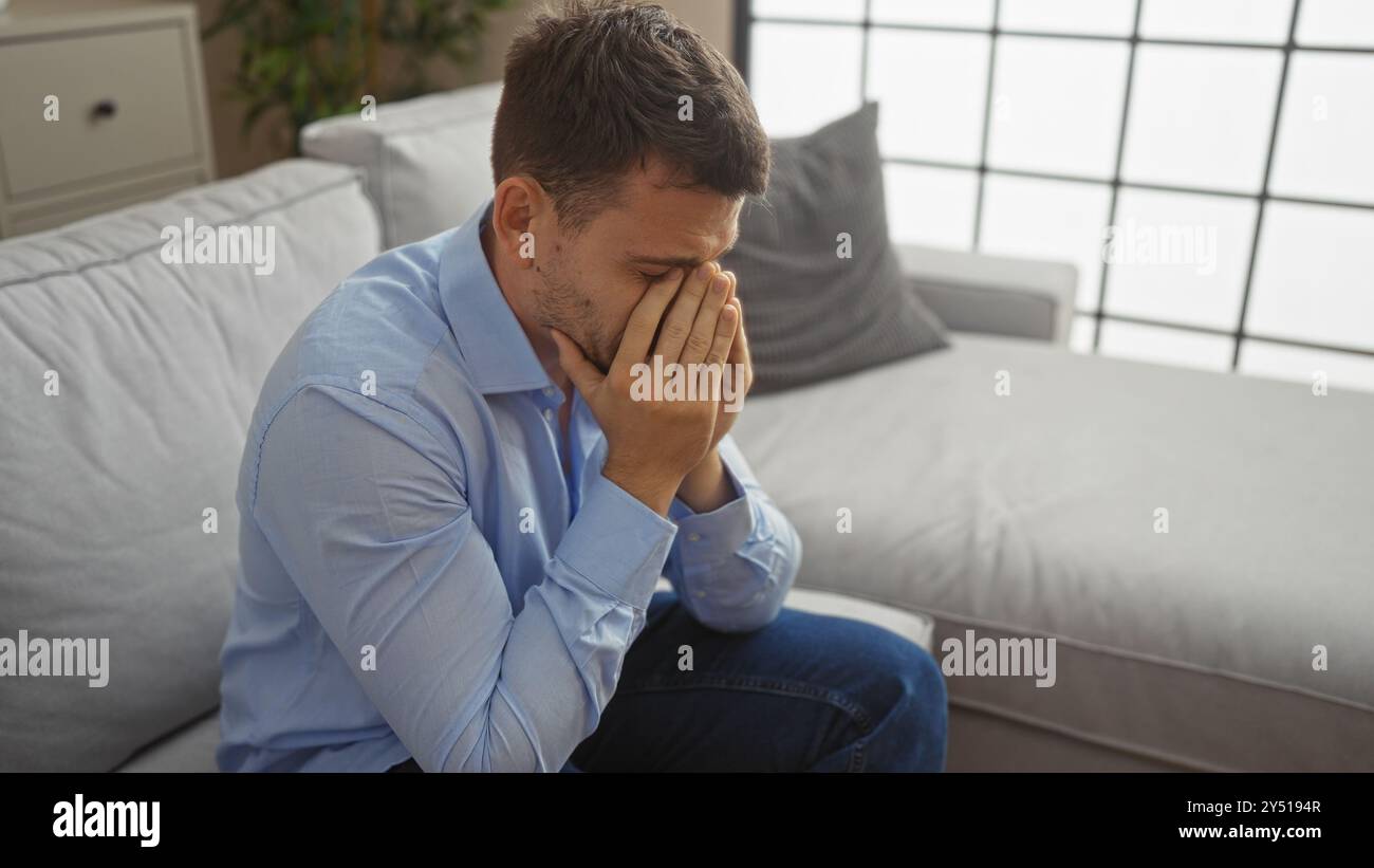 A distressed young hispanic man with a beard sitting in a modern living ...