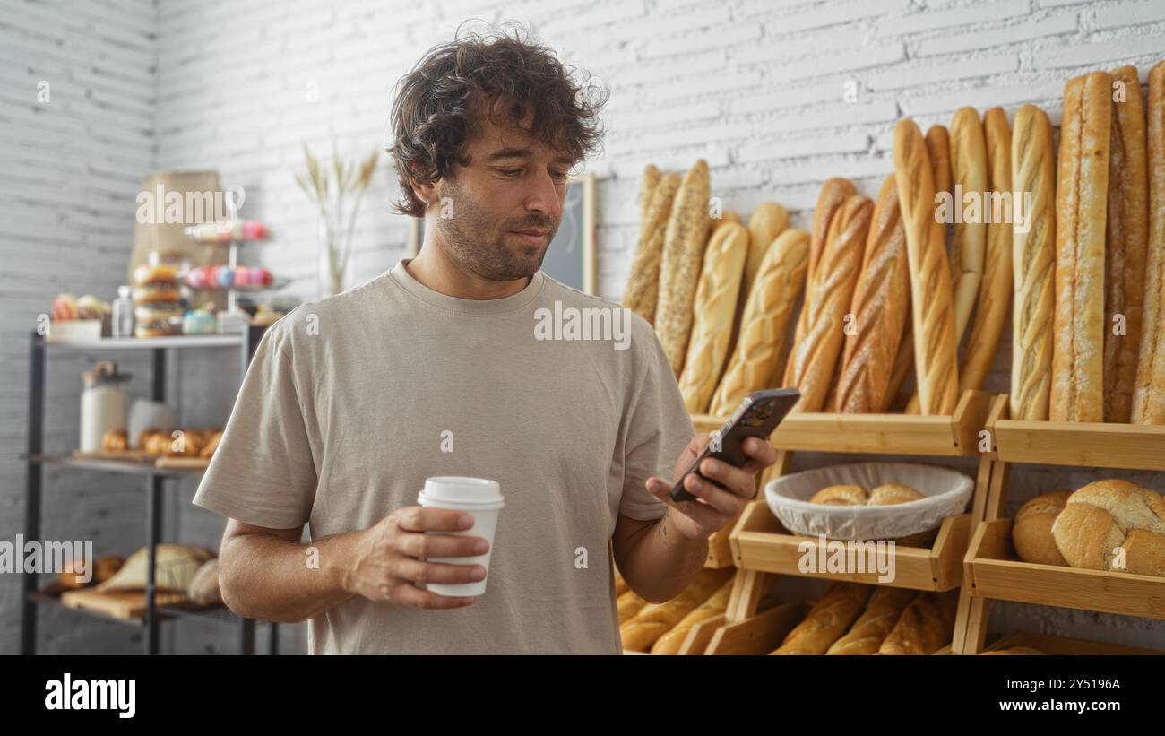 Young man holding coffee and phone in bakery shop interior with bread ...
