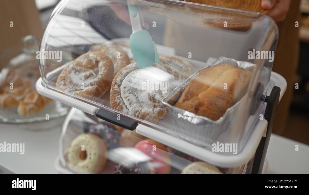Young man using tongs to select pastries from a display case in a ...