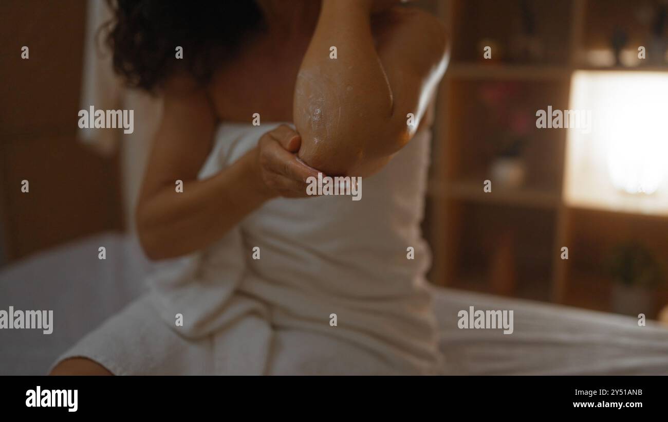 Woman relaxing in a spa room while applying lotion to her elbow ...