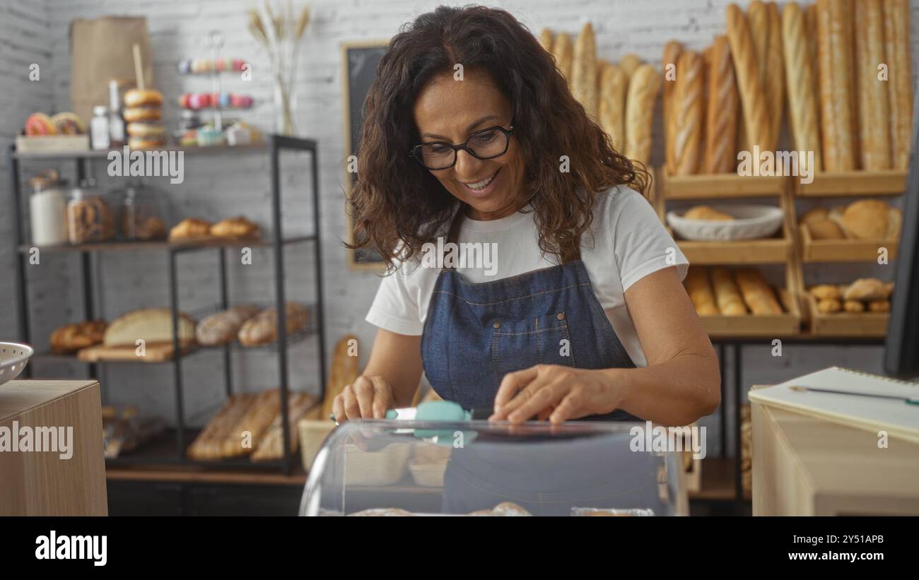 Middle-aged woman working in a bakery surrounded by fresh bread and ...